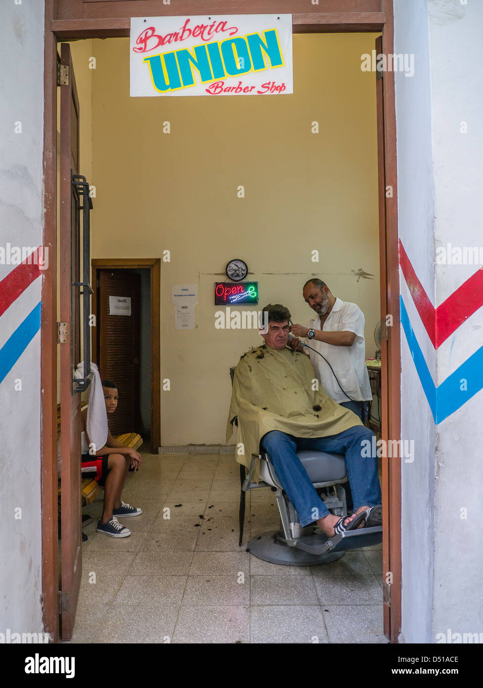 A Cuban barber cuts a middle-aged man's hair in his barber chair while ...