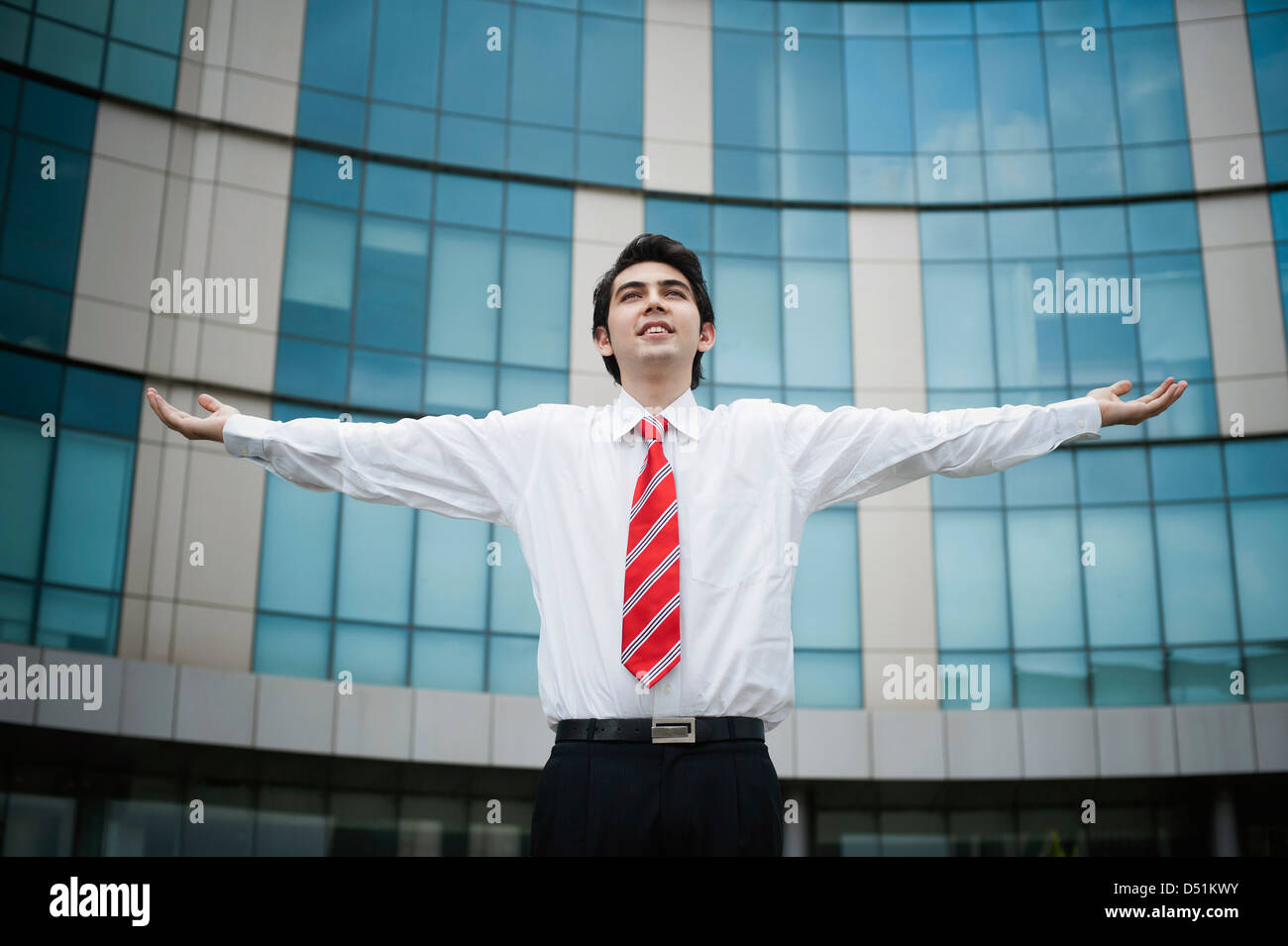 Man standing with his arms outstretched outside an office building ...