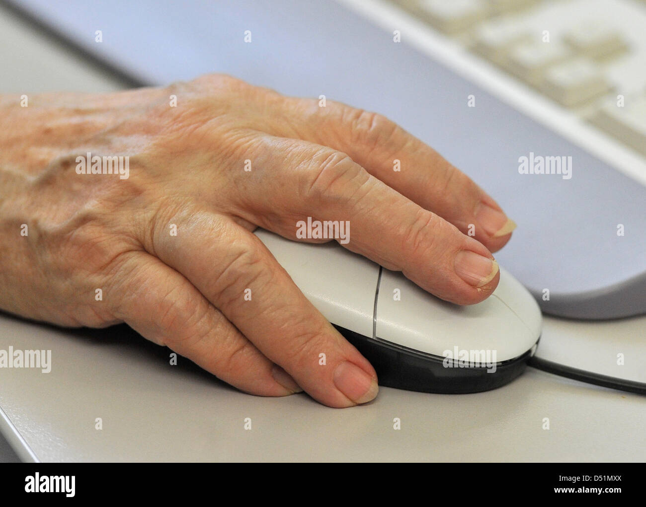 The hand of a senior citizen moves a computer mouse across a table ...