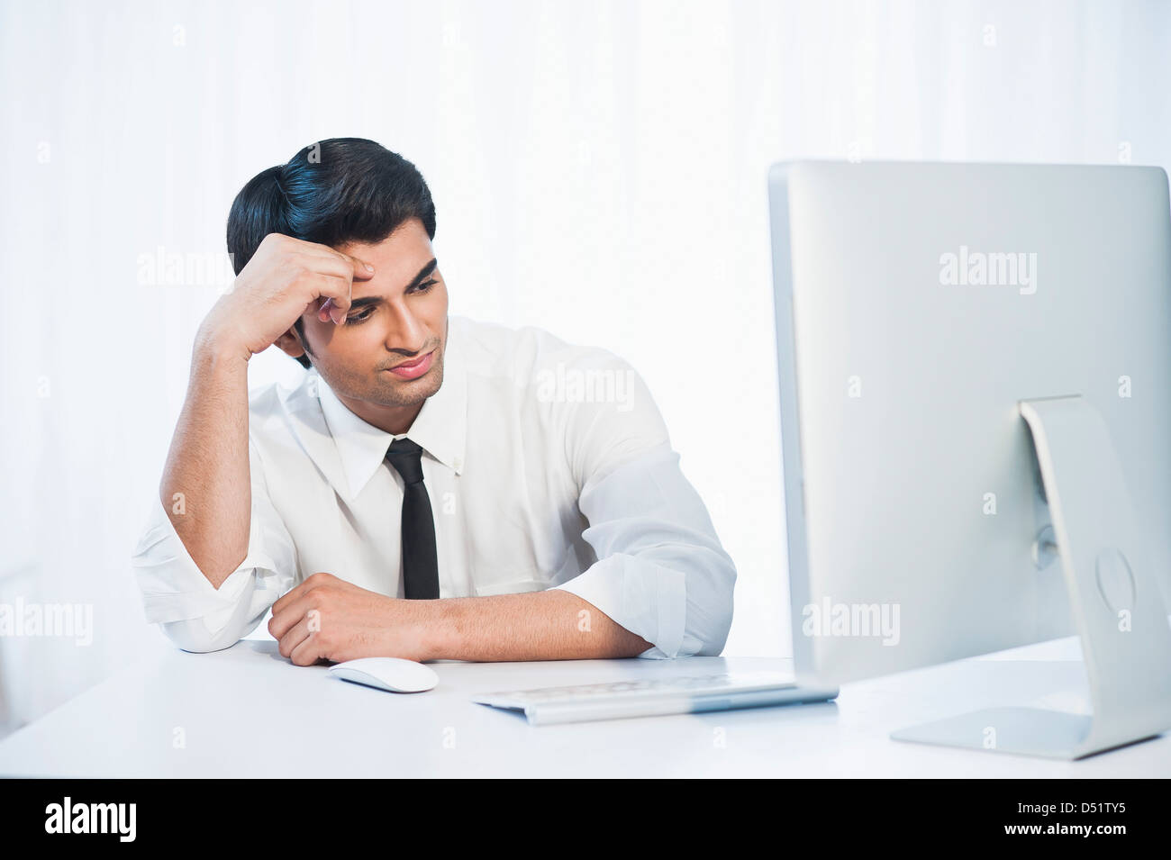 Businessman looking at a desktop pc and thinking Stock Photo - Alamy