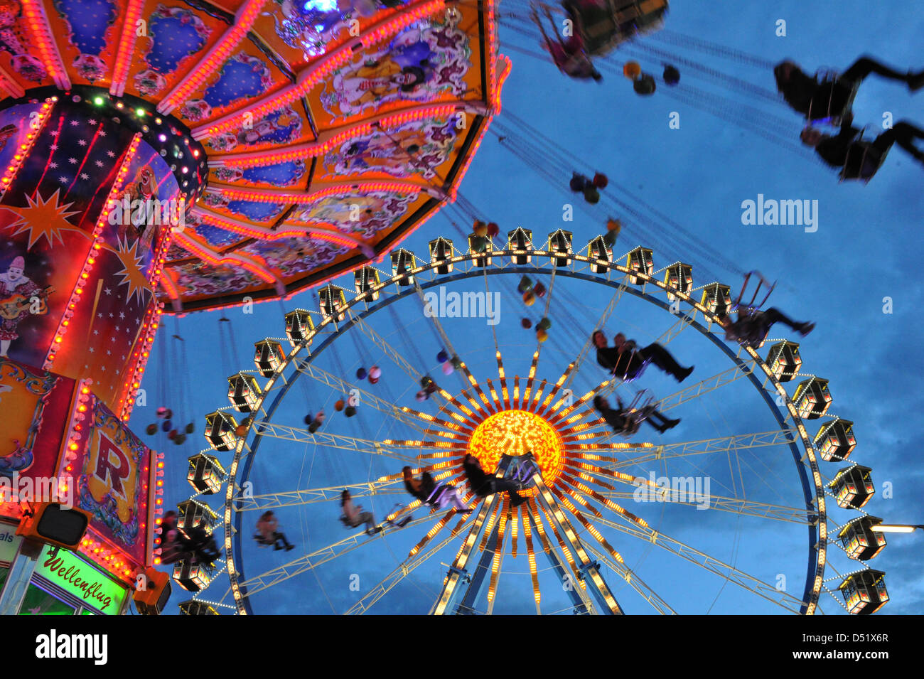 A ferris wheel and a carousel revolve in front of the evening sky at ...