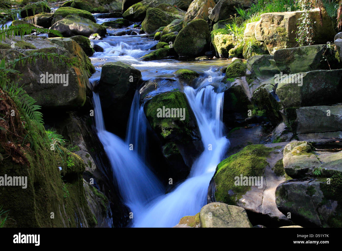 Slow shutter speed image of a small waterfall tumbling over mossy rocks ...