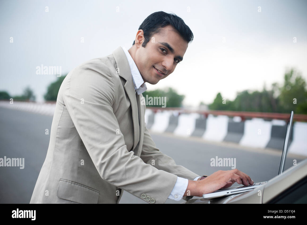 Businessman using a laptop on car bonnet and smiling at a flyover Stock ...