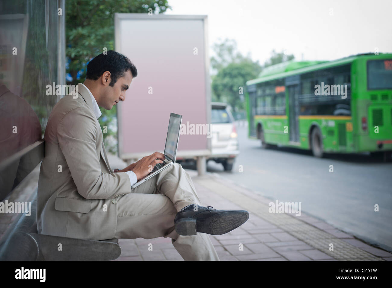 Businessman Sitting On A Bench At Bus Stop And Working On A Laptop