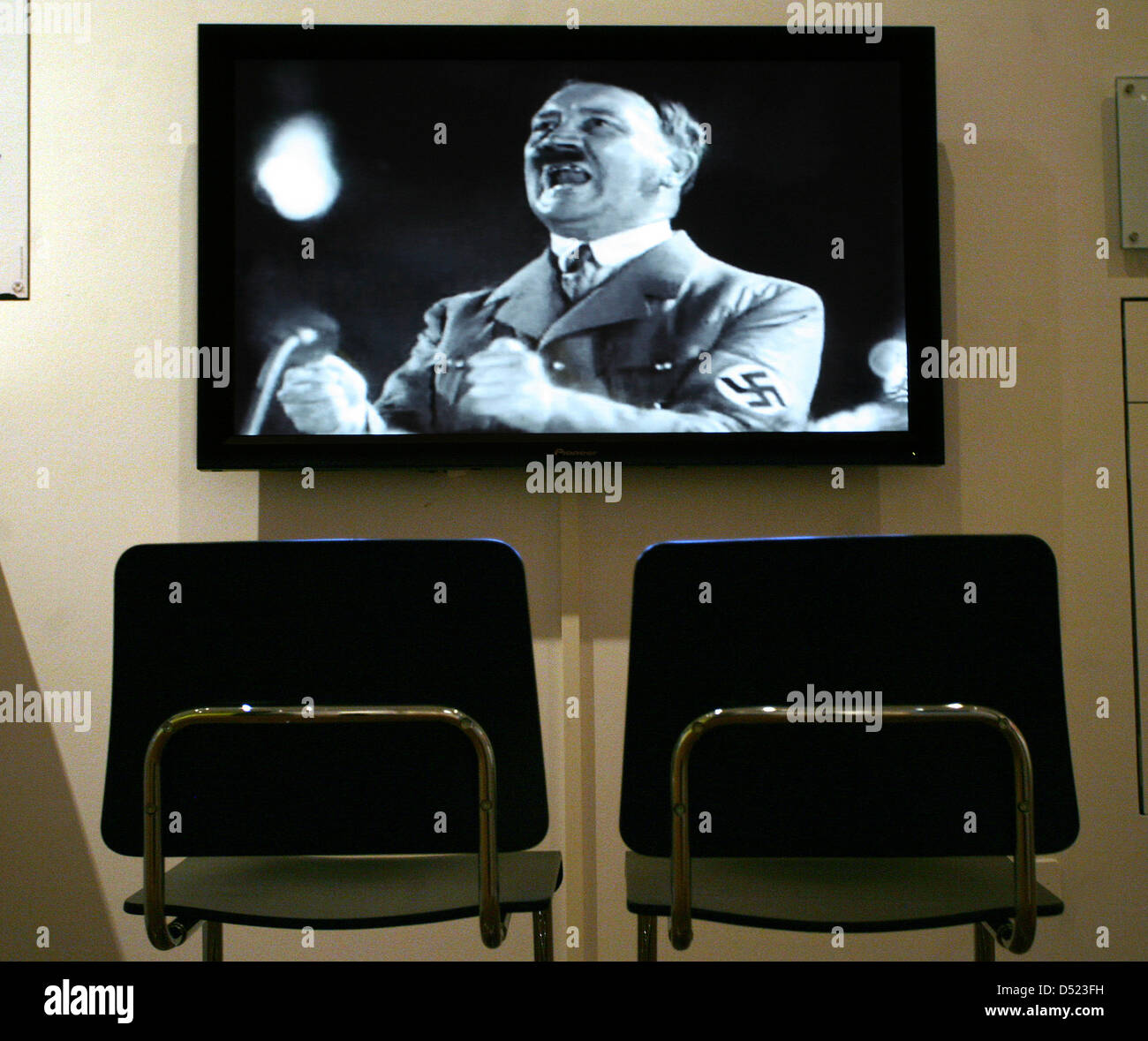 Two chairs sit in front of a screen that shows a speech of Hitler ...