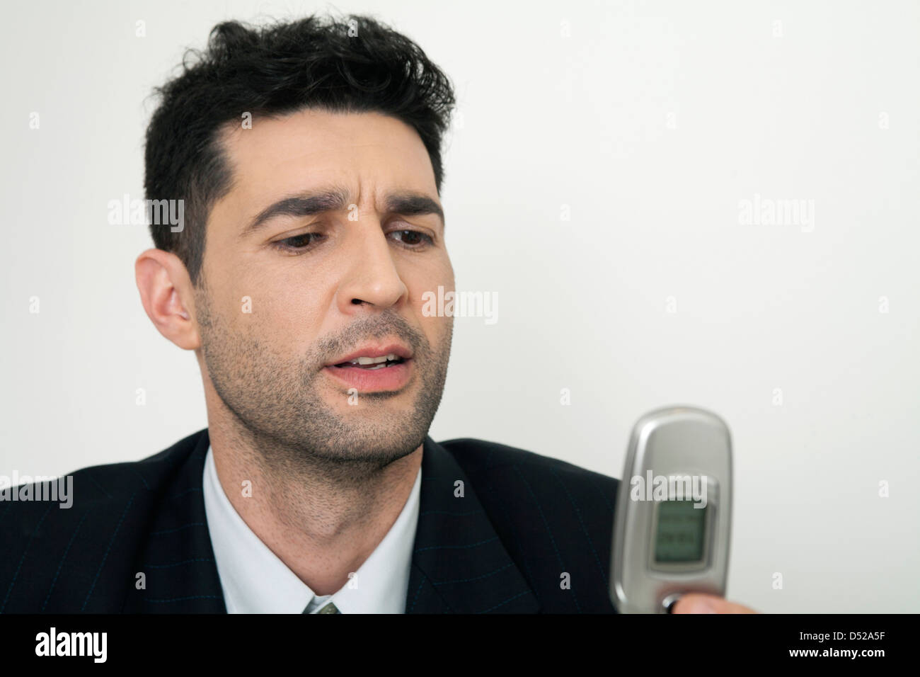 Mid-adult businessman looking at cell phone, frowning Stock Photo - Alamy