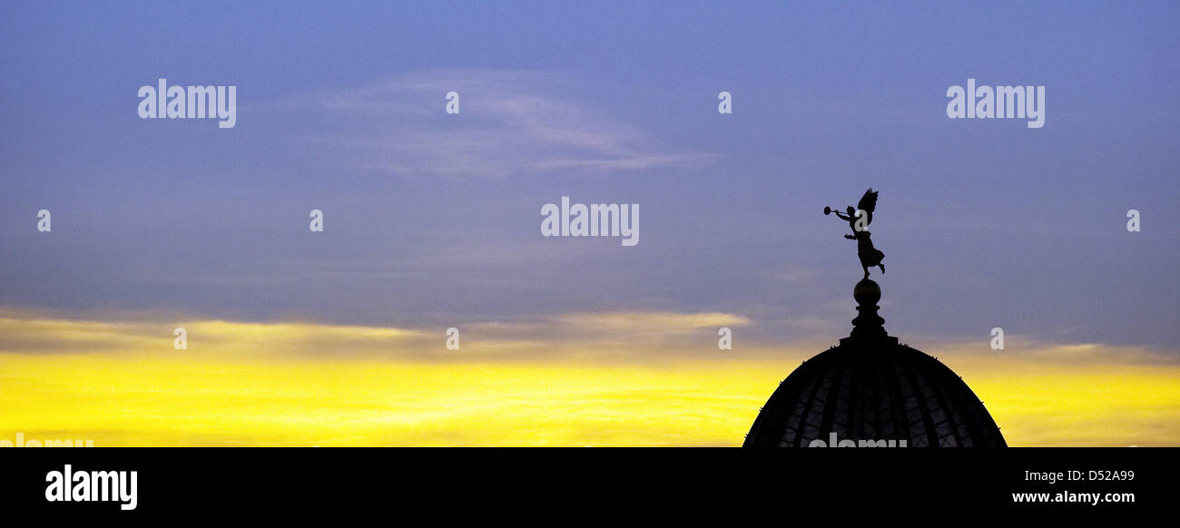 A statue of the goddess Fama is outlined against the dawn on top of the ...