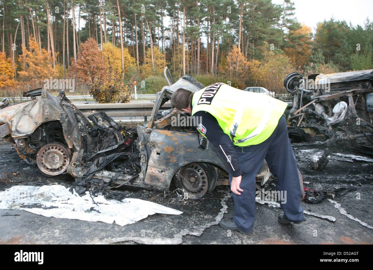 A policeman examines burnt-out vehicles after a severe car crash south ...