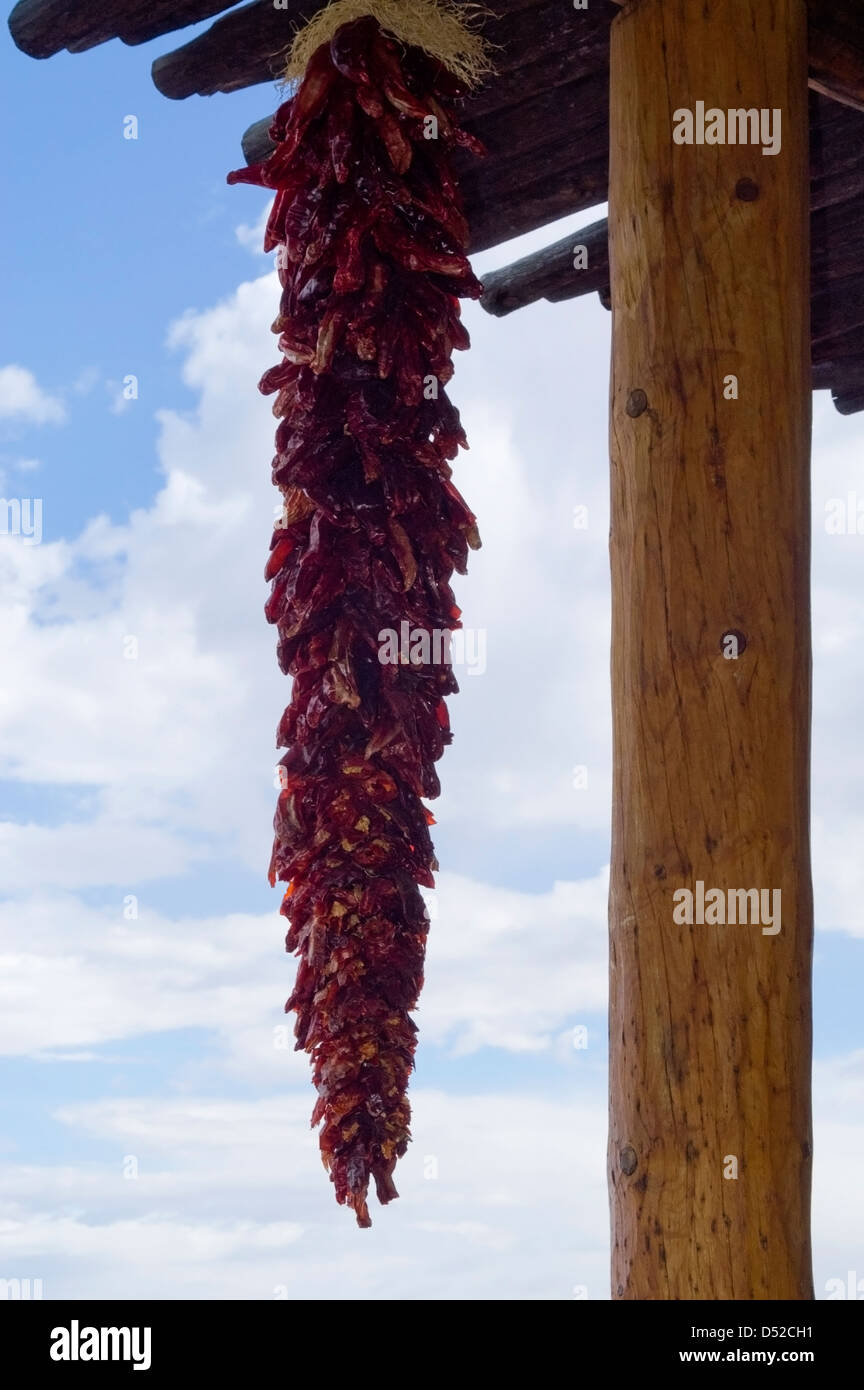 A very large chili pepper ristra hangs from the roof of a porch and ...
