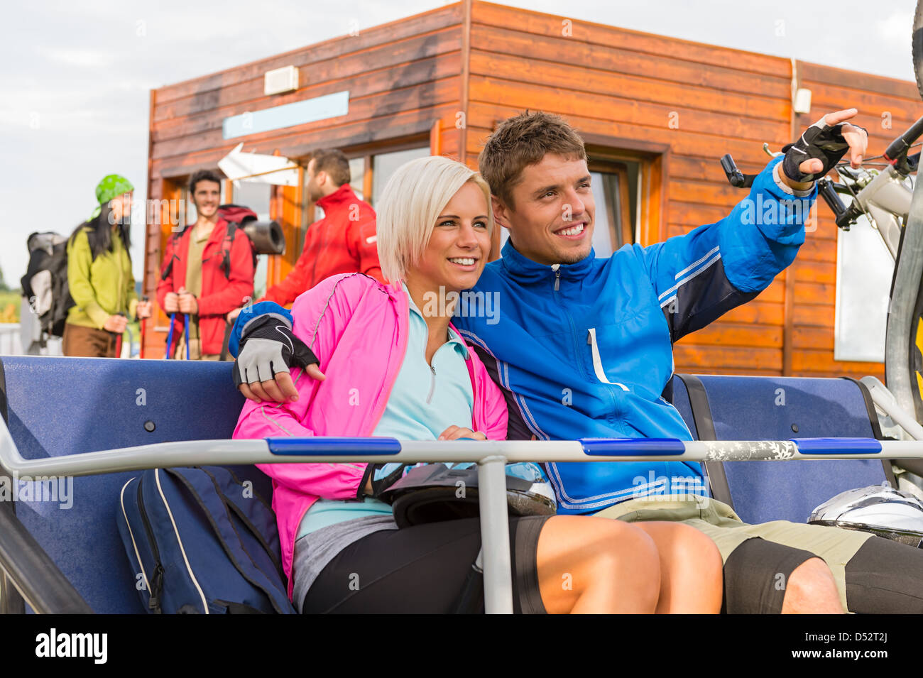 Cheerful couple sitting on chair lift man pointing Stock Photo - Alamy
