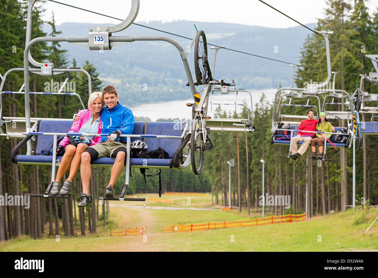 Smiling couples using chair lift in scenic landscape Stock Photo - Alamy