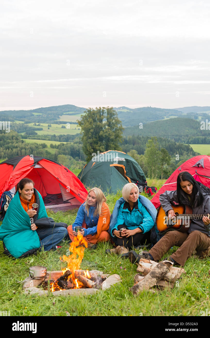 Young girls camping with tents beside campfire in nature landscape ...