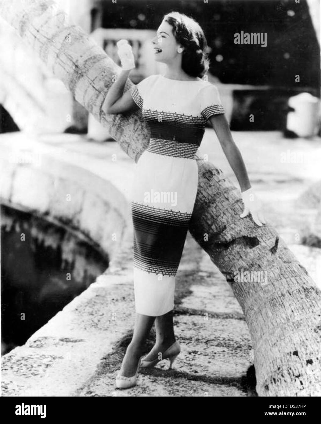 A fashion model standing against tree trunk poses for a photo Stock ...