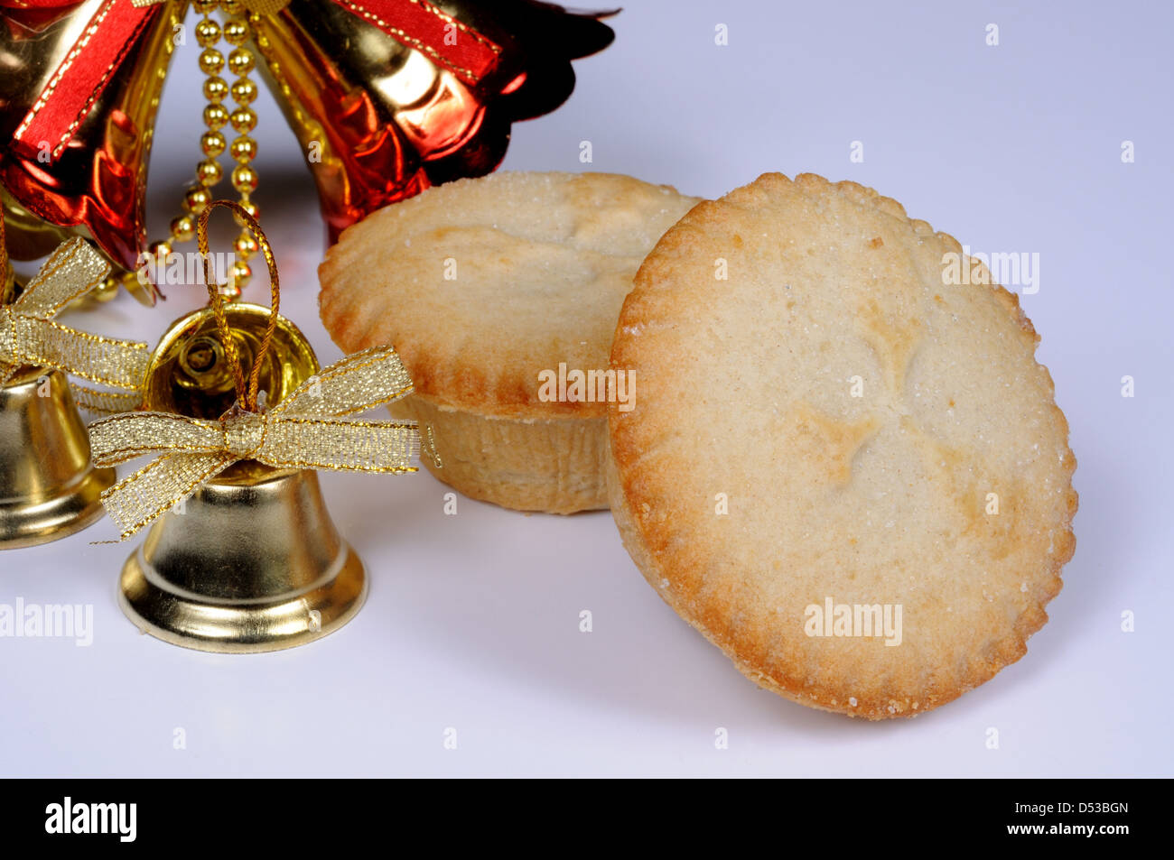 Two mince pies with Christmas bells to the rear against a grey ...