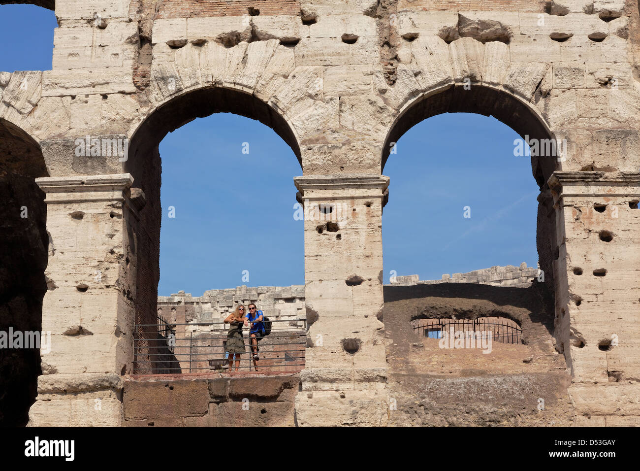 Young couple standing in the arches of the Coliseum wall looking out at ...