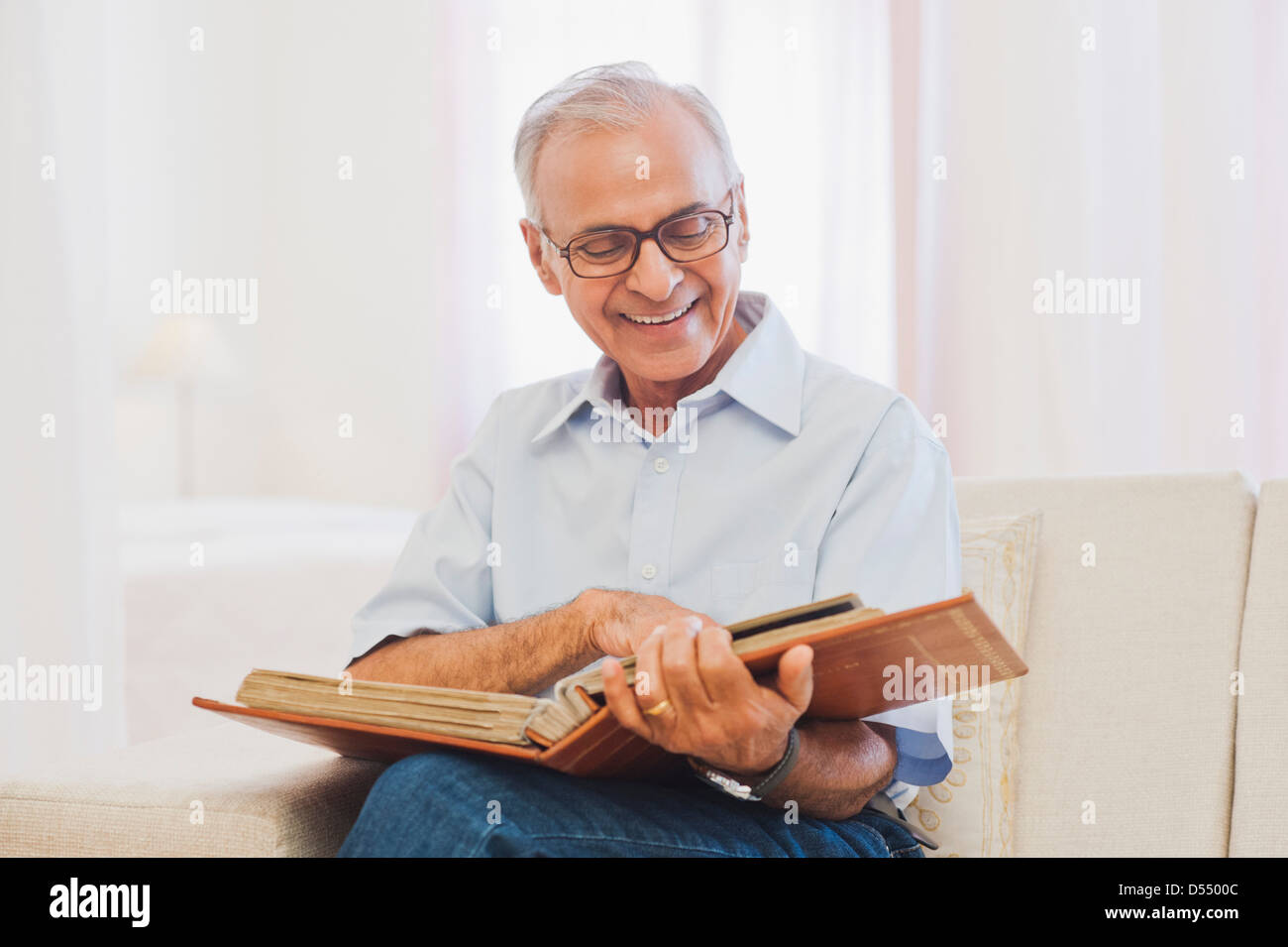 Senior man sitting on a sofa and watching photo album Stock Photo - Alamy