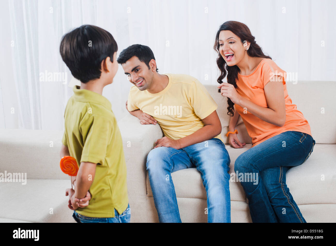 Boy hiding candy behind his back with his parents try to looking at ...