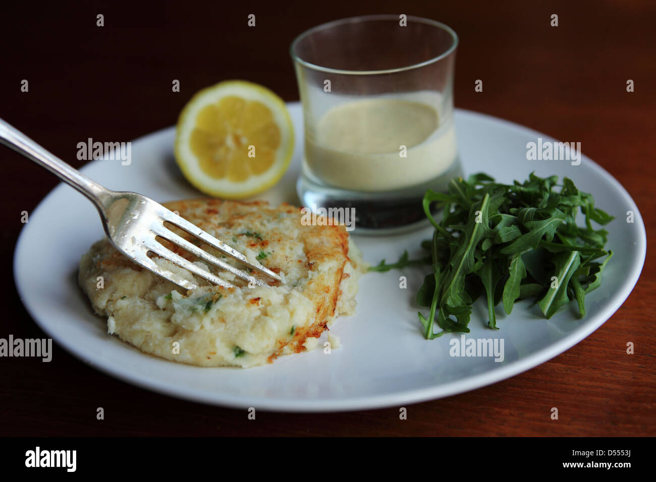 Fish cake served with a wedge of lemon, rocket (ruccola) salad and ...
