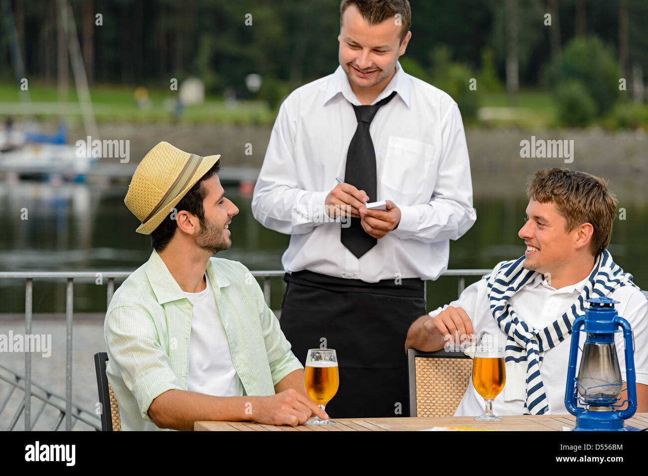 Smiling waiter taking order from men customers outdoor bar Stock Photo ...