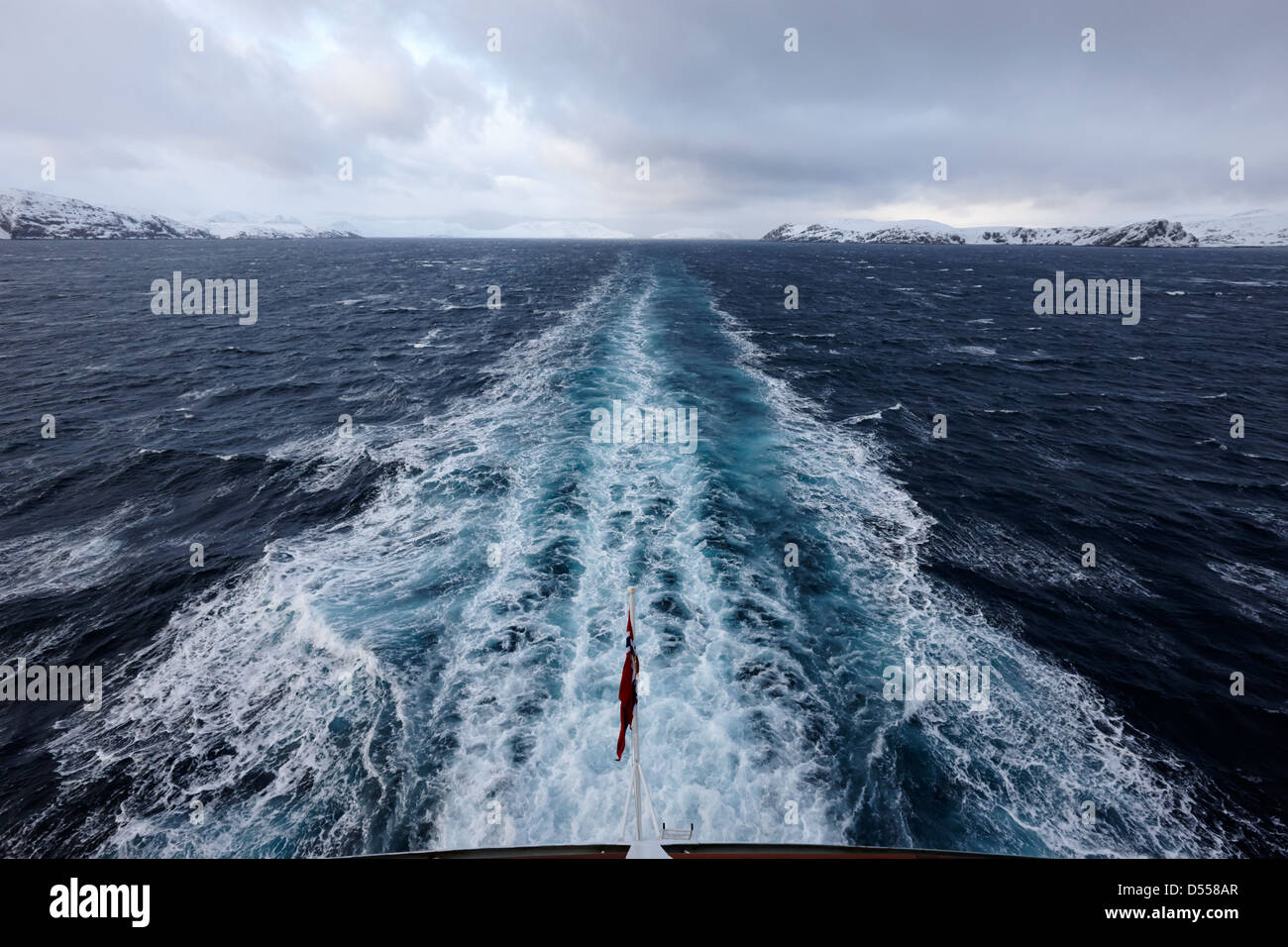 ships wake in the sea with snow covered cliffs and rugged arctic ...
