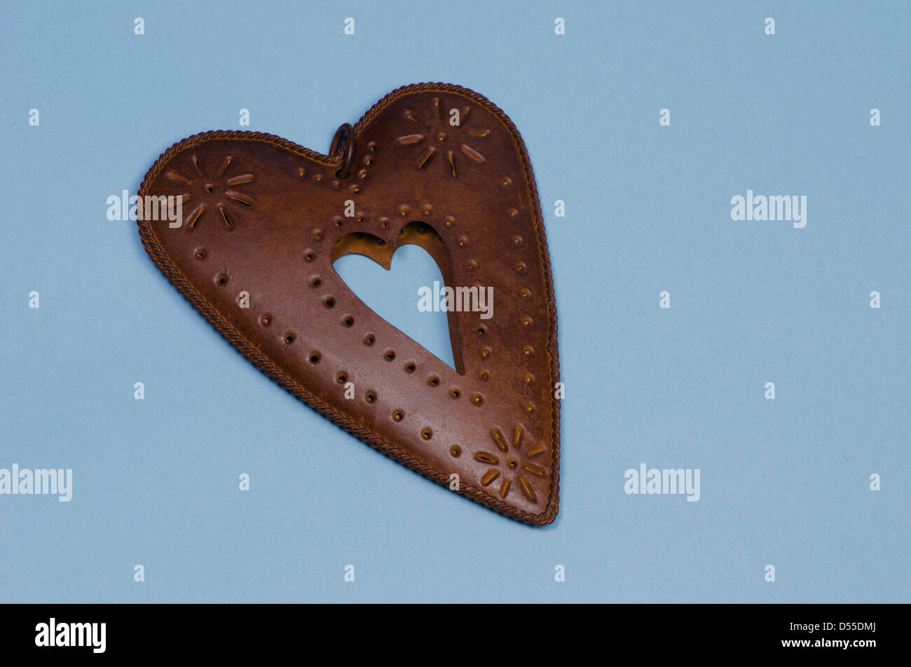 A rusty metal heart is photographed on a light blue background, with ...