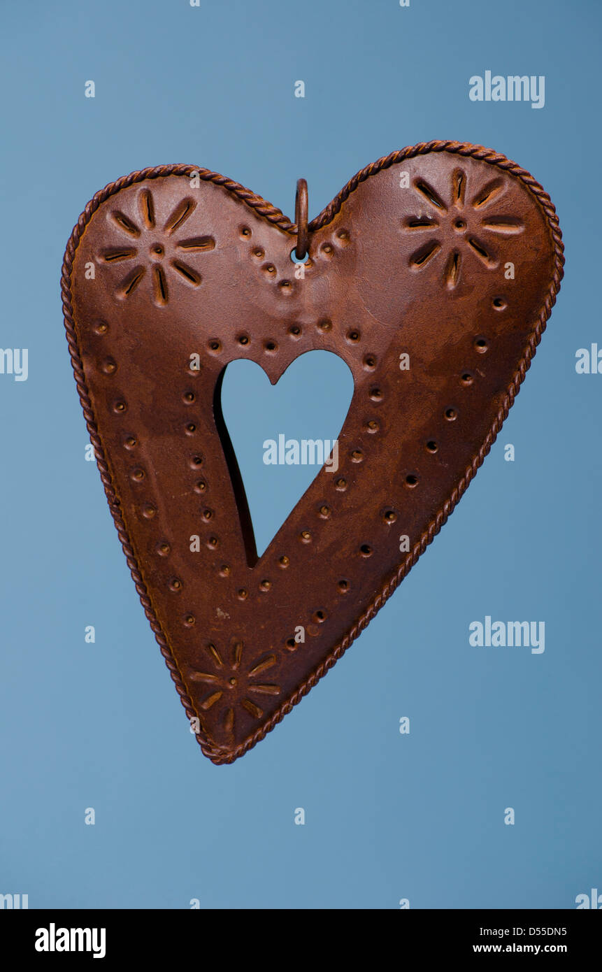 A rusty metal heart is photographed on a light blue background, with ...