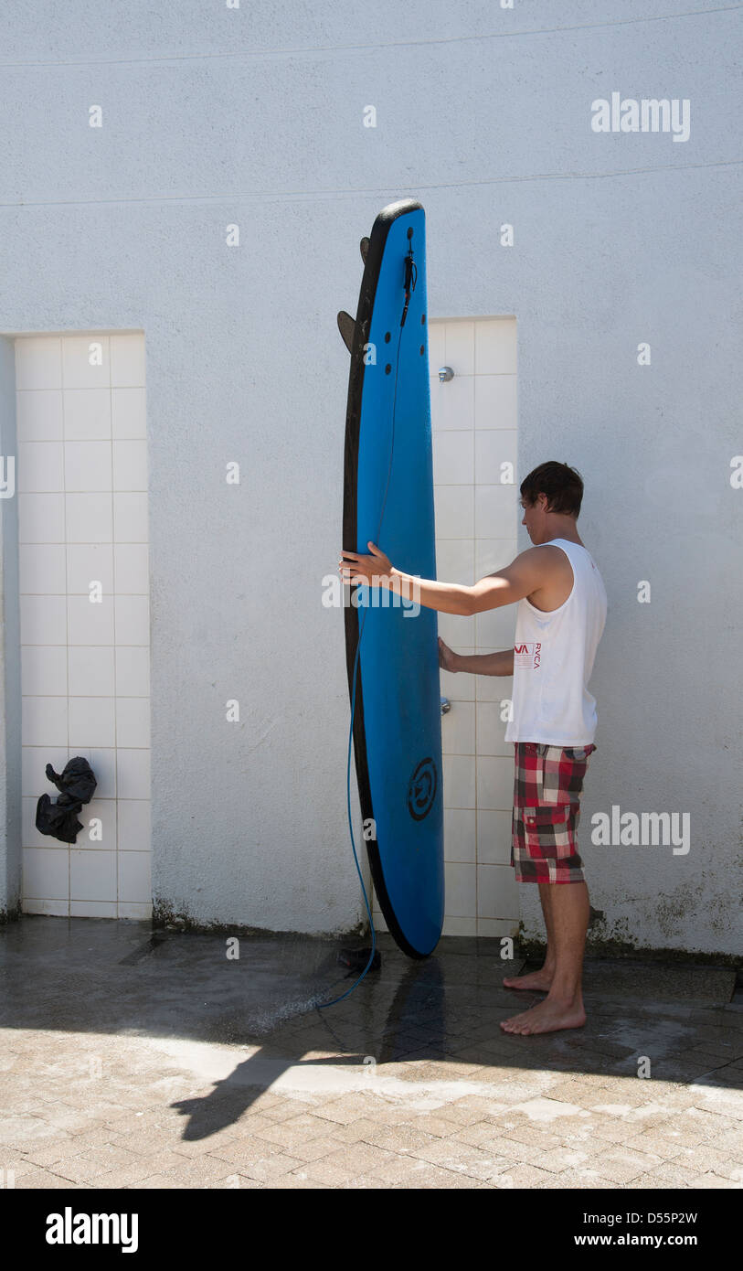 Young surfboarder washing the seawater of his board in the gents toilet ...
