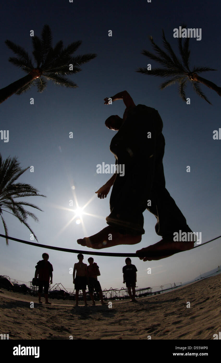 A young man practice slackline on the beach. Slacklining is a practice ...