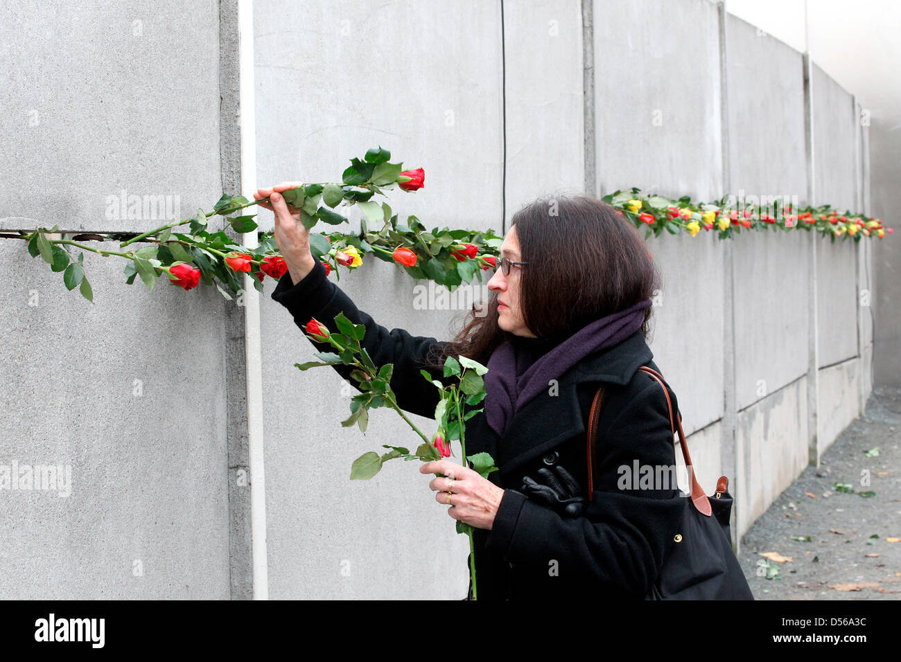A woman sticks a rose into a crack of the wall at Bernauer Street ...