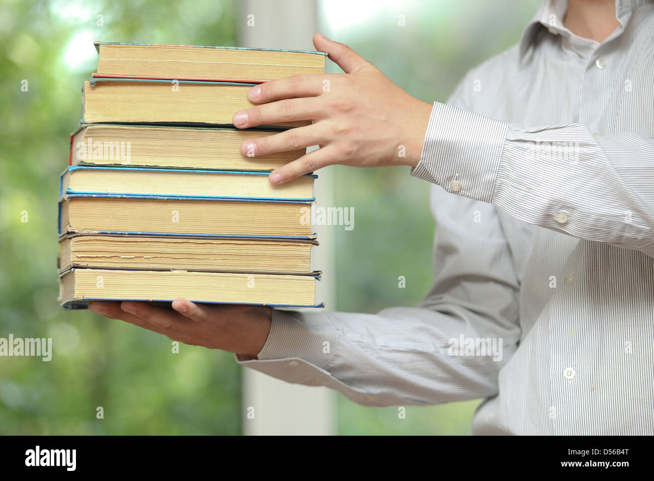 Guy in a shirt holding a stack of old books Stock Photo - Alamy