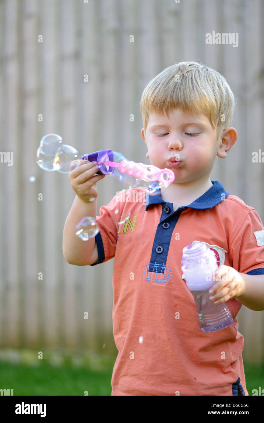 little boy having fun blowing bubbles in the garden on a summer day ...
