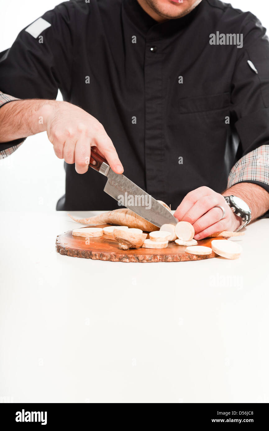 Close-up of the hands of a cook cutting raw ingredients on a wooden ...