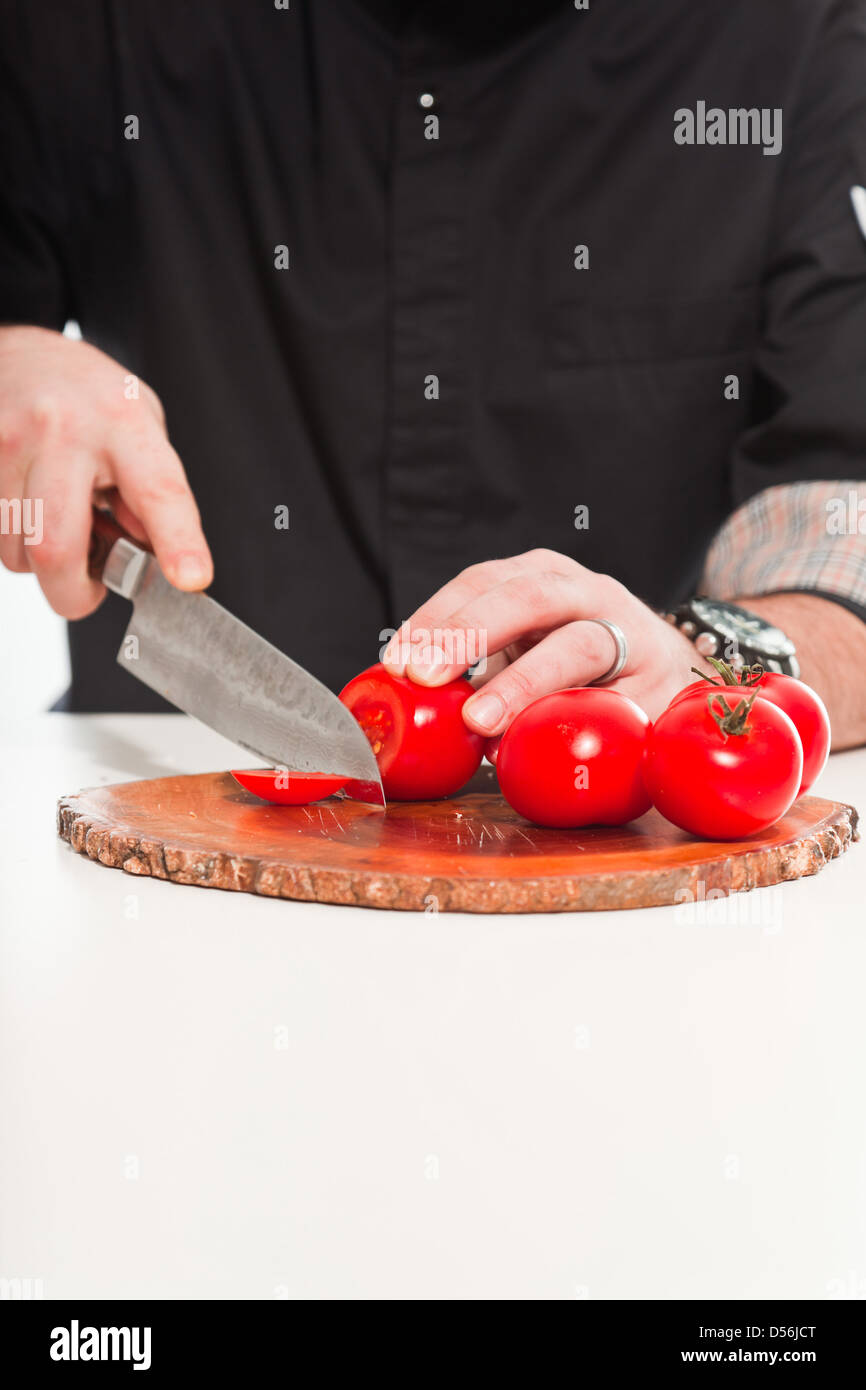 Close-up of the hands of a cook cutting raw ingredients on a wooden ...