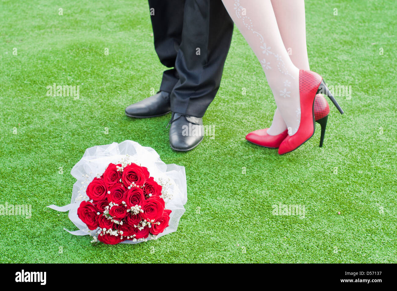 legs of bride and fiancé on the green grass with wedding red bouquet ...