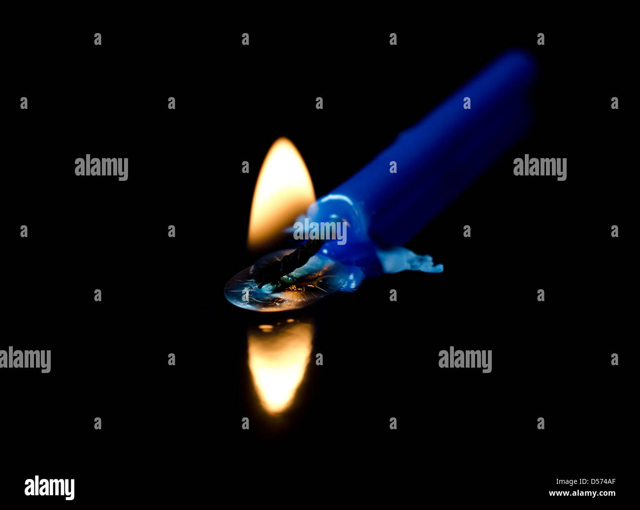 A burning blue birthday candle lying on it's side on a reflective ...