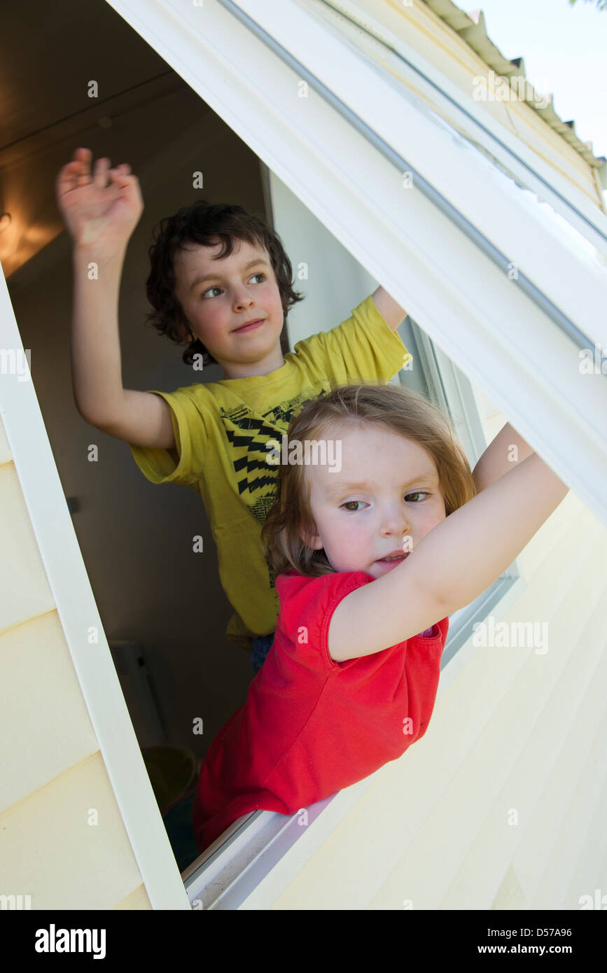 Young siblings looking out open window Stock Photo - Alamy