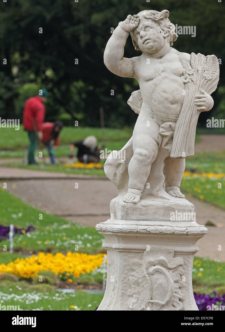 Behind an angel statue, three gardeners work in the Baroque Garden of ...