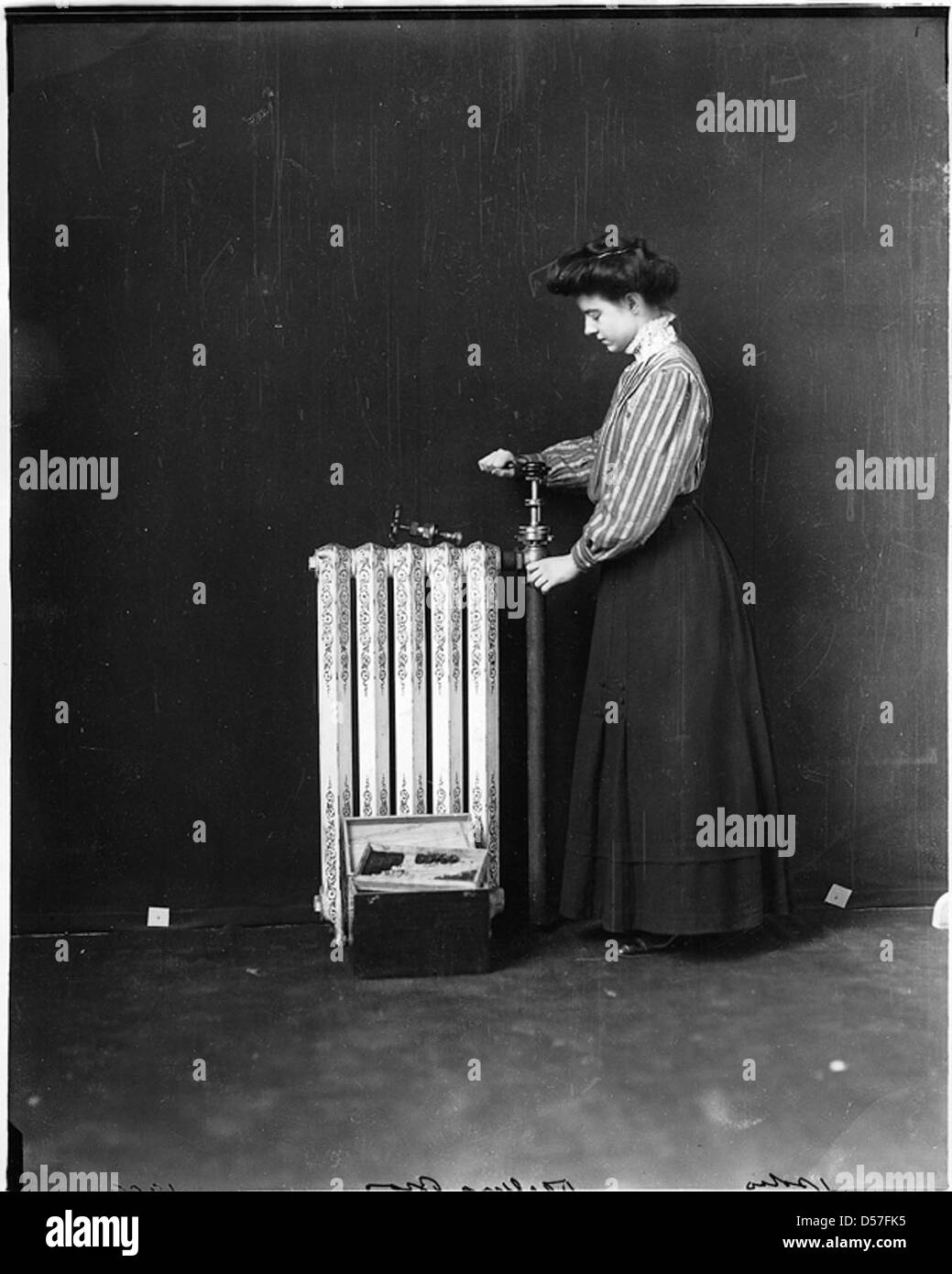 A photograph from 1909 showing a woman repairing a hot water radiator ...