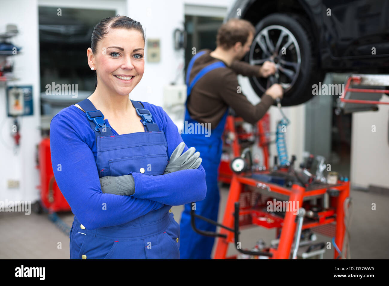 Female mechanic standing in workshop, another mechanic changes a wheel ...
