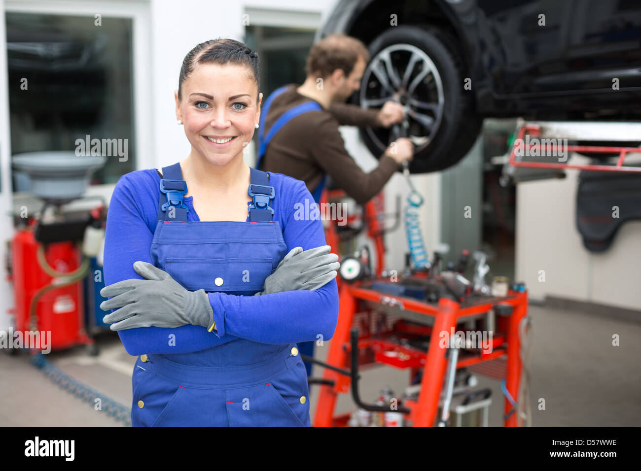 Female mechanic standing in workshop, another mechanic changes a wheel ...