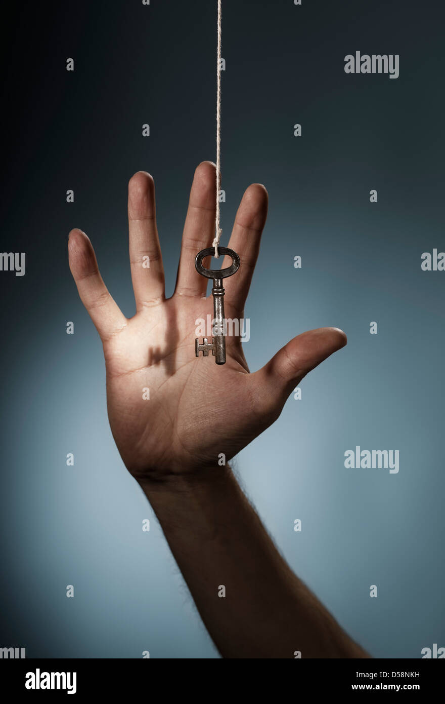A Key hanging from a string in front of a hand Stock Photo - Alamy