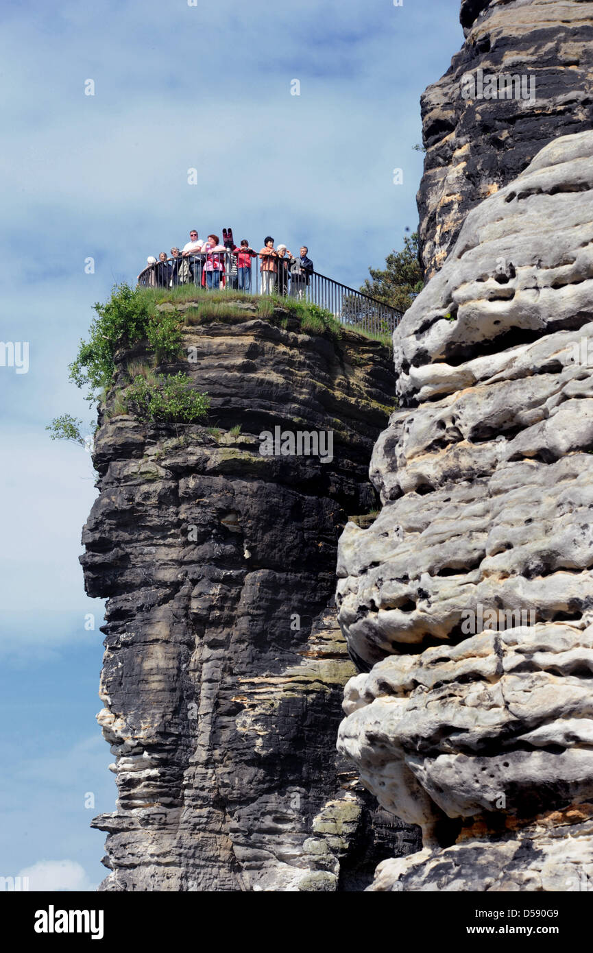 A group of tourists stand on the platform on top of a cliff, the so ...