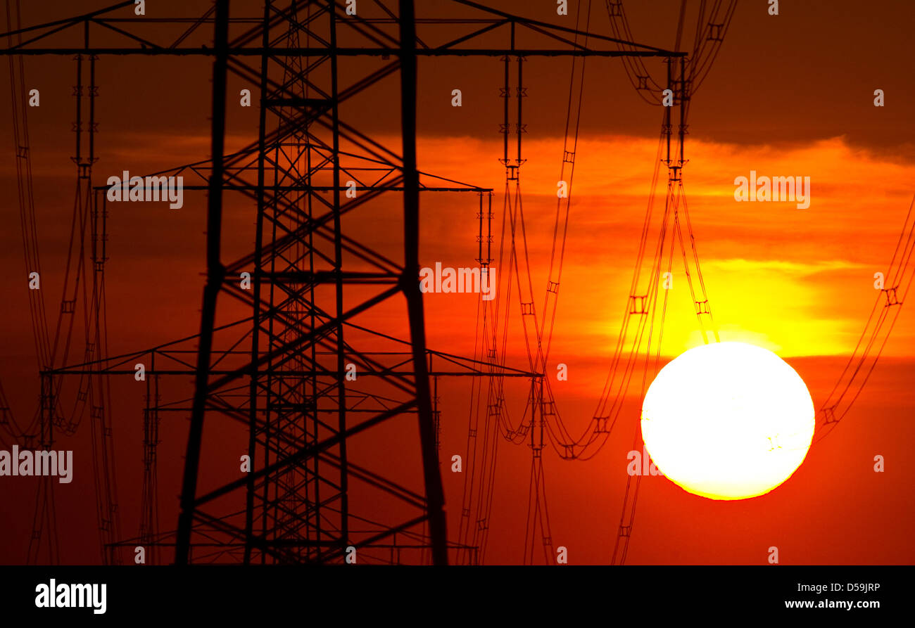 The evening sun sets colourfully behind utility poles on a field close ...