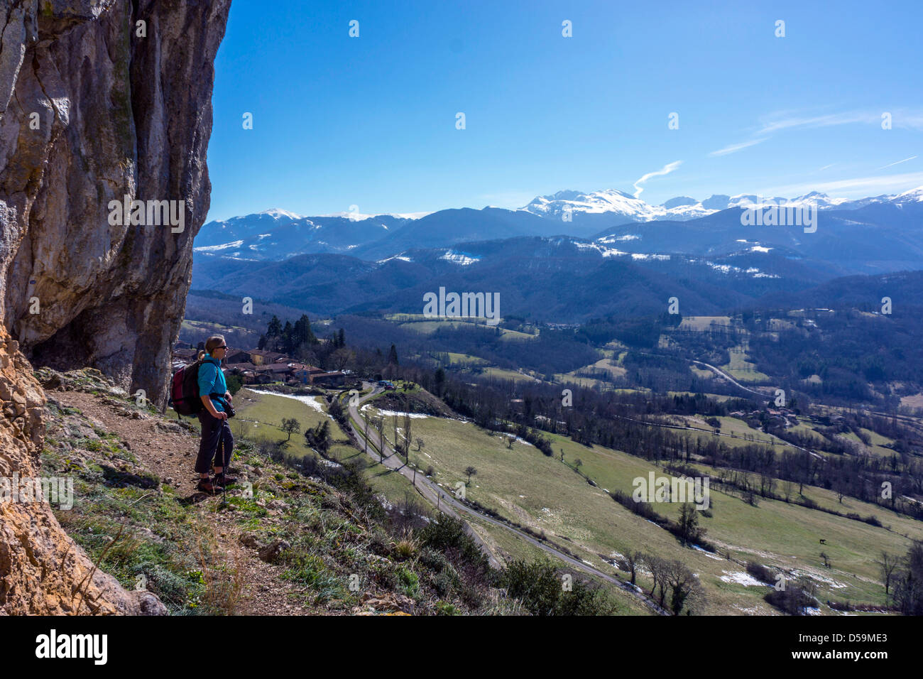 Figure in blue, with view towards snowy Pyrenees from below rock face ...