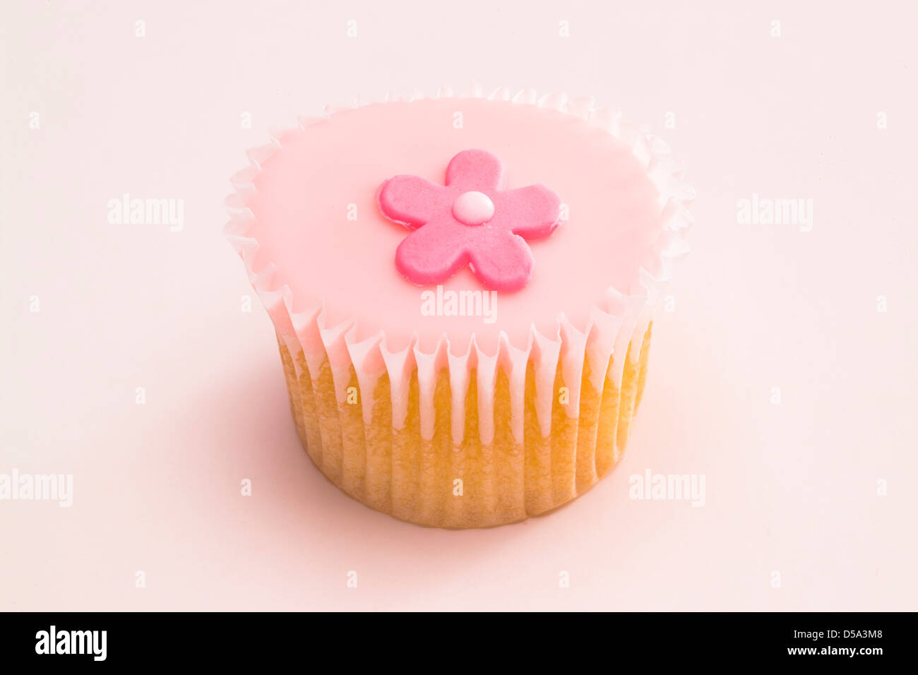 Single iced cupcake decorated with a pink flower on a white background ...