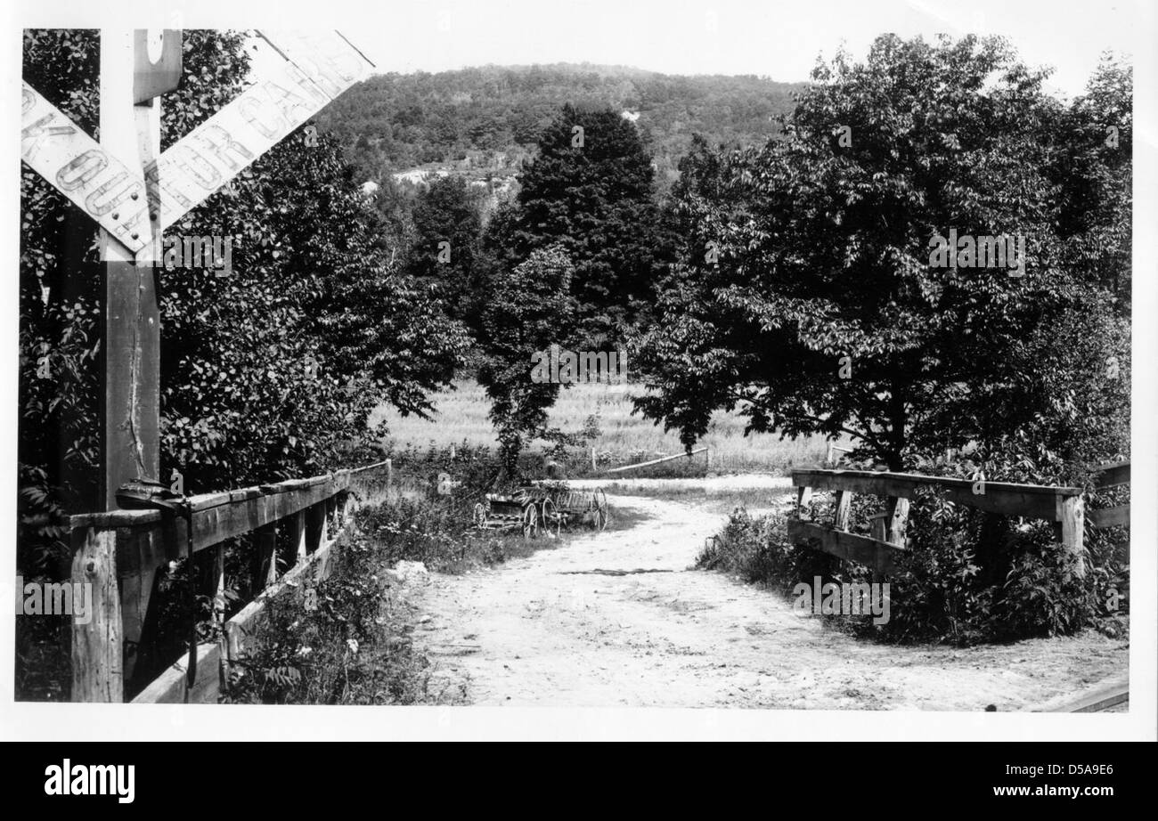 A rural scene depicting a railroad crossing, with tracks passing ...