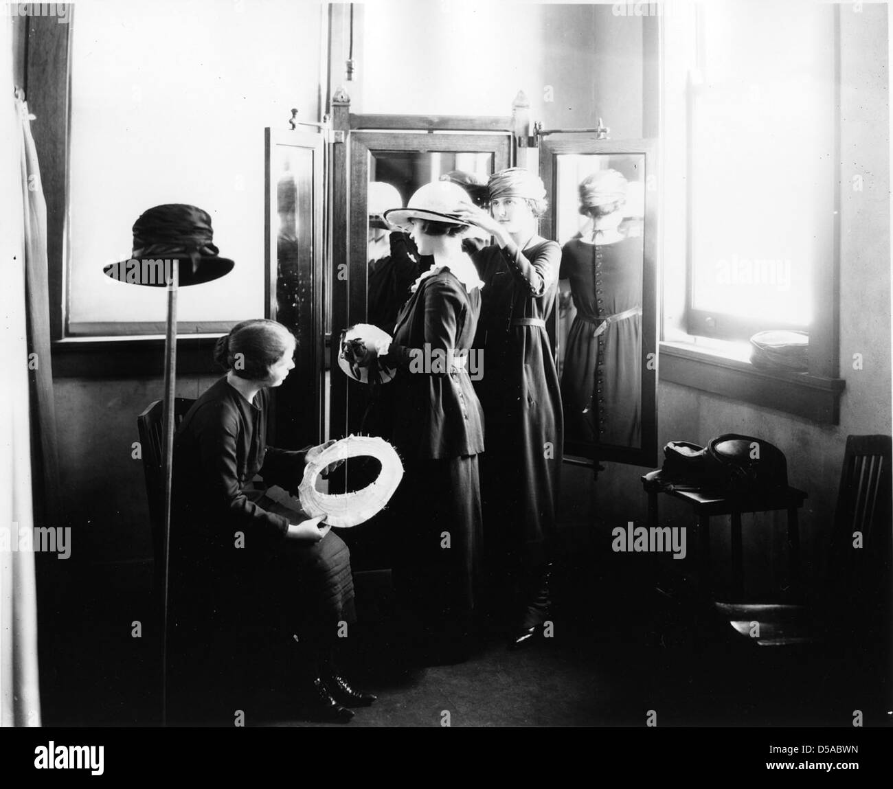 This photograph captures students fitting millinery in a home economics ...
