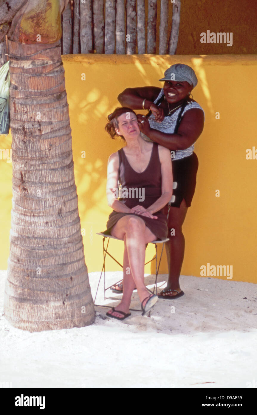 A female tourists receives a hair braiding on caye caulker, Belize ...