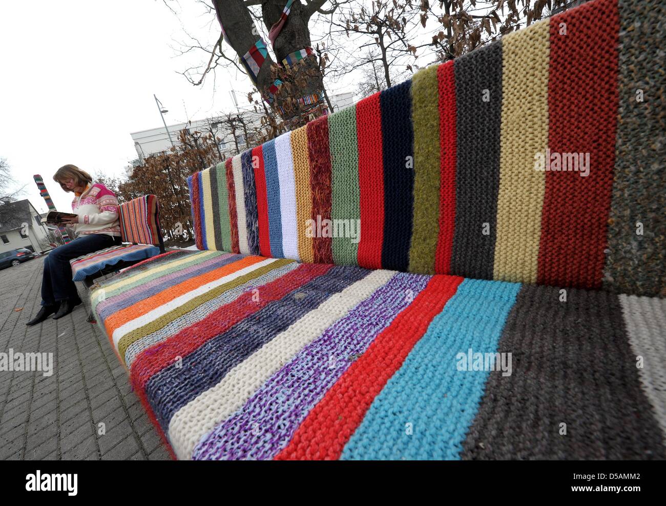 A woman sits on a bench which has a knitted covering in Hanover ...