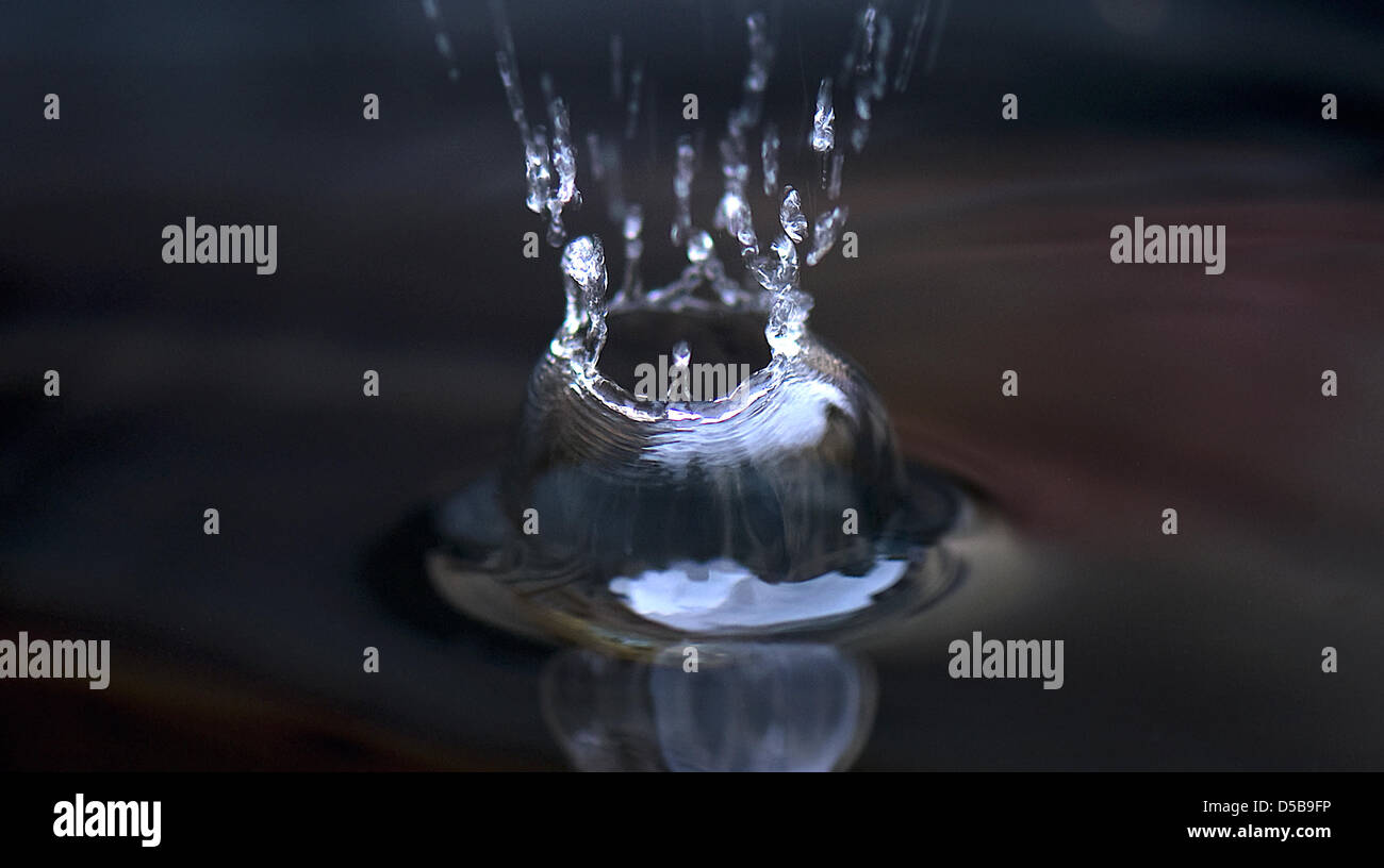 A drop of water hits the surface of rain water collected in a water ...